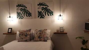 Quarto com cama, duas luminárias fixadas na parede e uma televisão sobre uma prateleira.