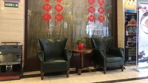 Um hall com duas poltronas de couro, uma mesa pequena com um vaso vermelho e uma parede grande decorada em vermelho.