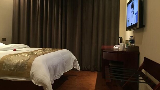 Quarto de hotel com cama, cortinas, televisão e uma pequena mesa com uma cadeira.
