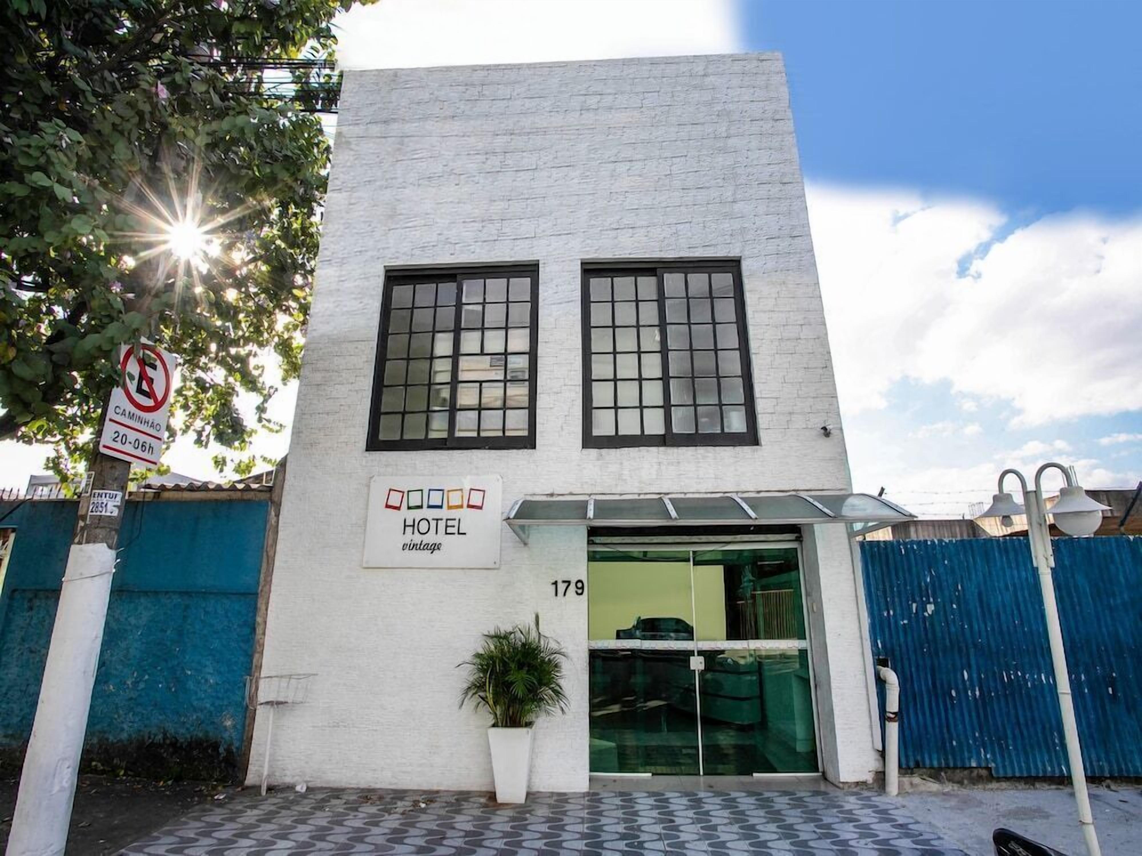 Um edifício com fachada branca, duas janelas grandes e uma placa indicando que é um hotel.