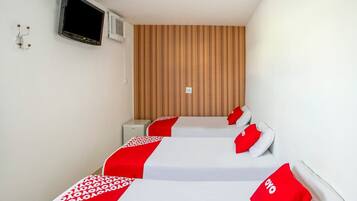 Quarto de hotel com duas camas, cada uma com roupa de cama vermelha e branca, uma televisão na parede e painel de parede de madeira.