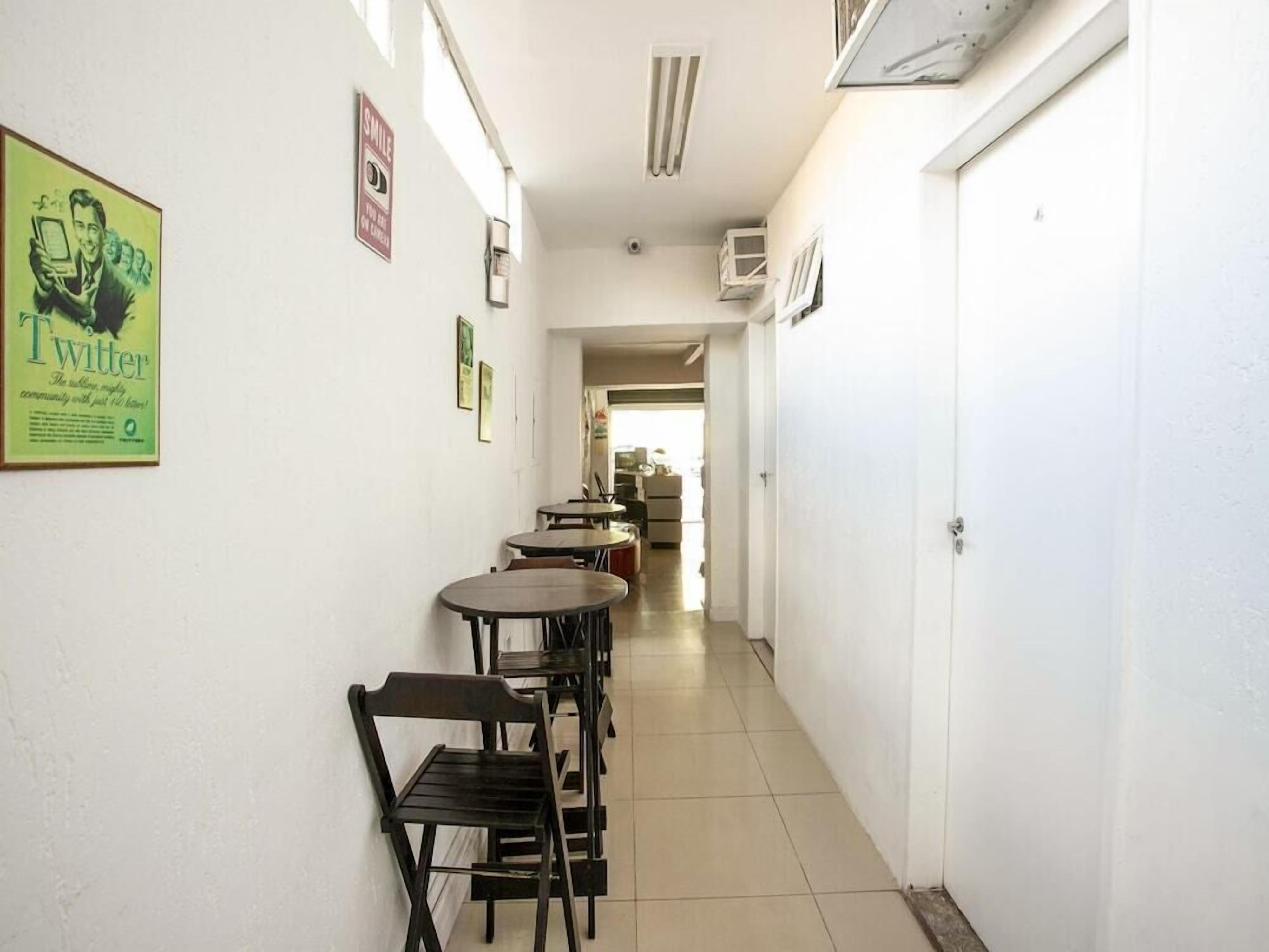Um corredor com mesas, cadeiras, uma porta e um cartaz na parede.