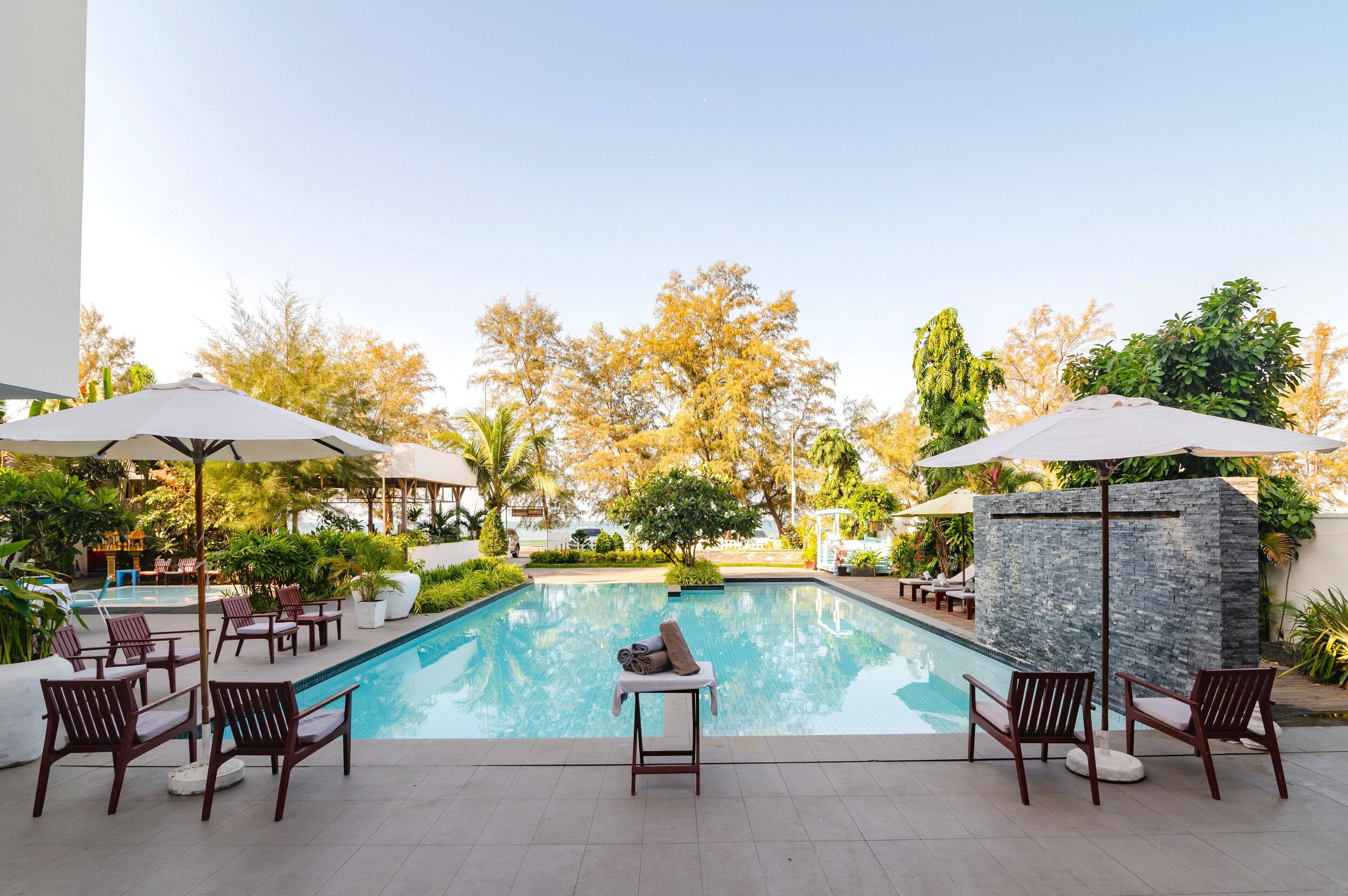 Piscina com espreguiçadeiras e guarda-sóis, rodeada por vegetação e árvores.