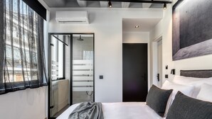 Quarto moderno com uma cama grande, uma porta de correr de vidro que dá para um banheiro e um quadro abstrato de grandes dimensões na parede.