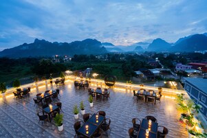 Um restaurante no terraço com área externa, plantas em vasos e vista para montanhas.