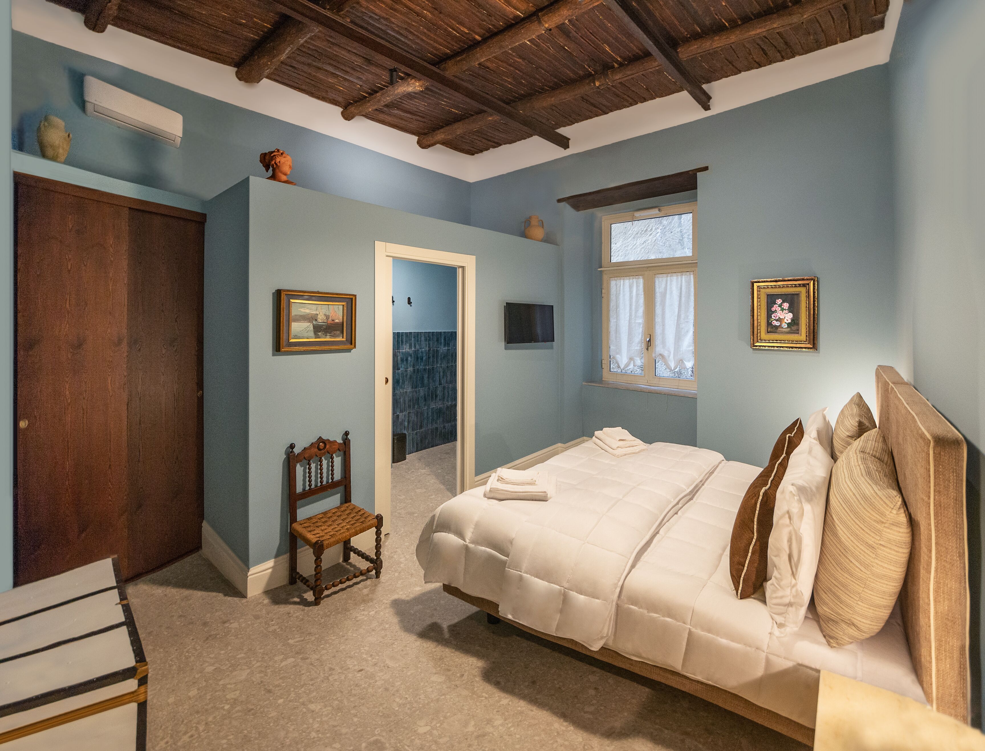 Quarto com cama de madeira, uma cadeira, guarda-roupa, janela e porta.