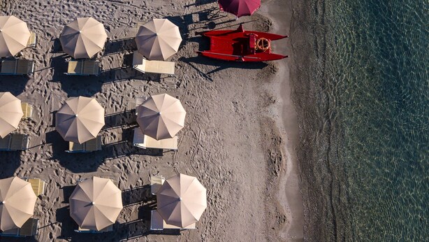 Vista aérea de uma praia com vários guarda-sóis e cadeiras de praia dispostas em fileiras.