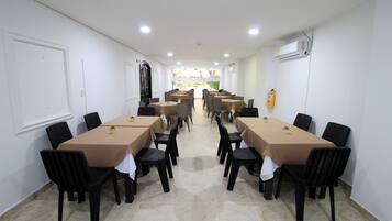 Uma sala de conferências com várias mesas e cadeiras, paredes brancas e chão em mosaico.
