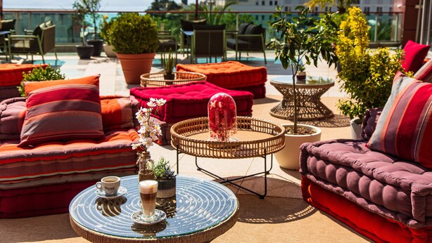 Terraço no telhado com área de estar ao ar livre, plantas em vasos e vista para edifícios e um corpo d'água.