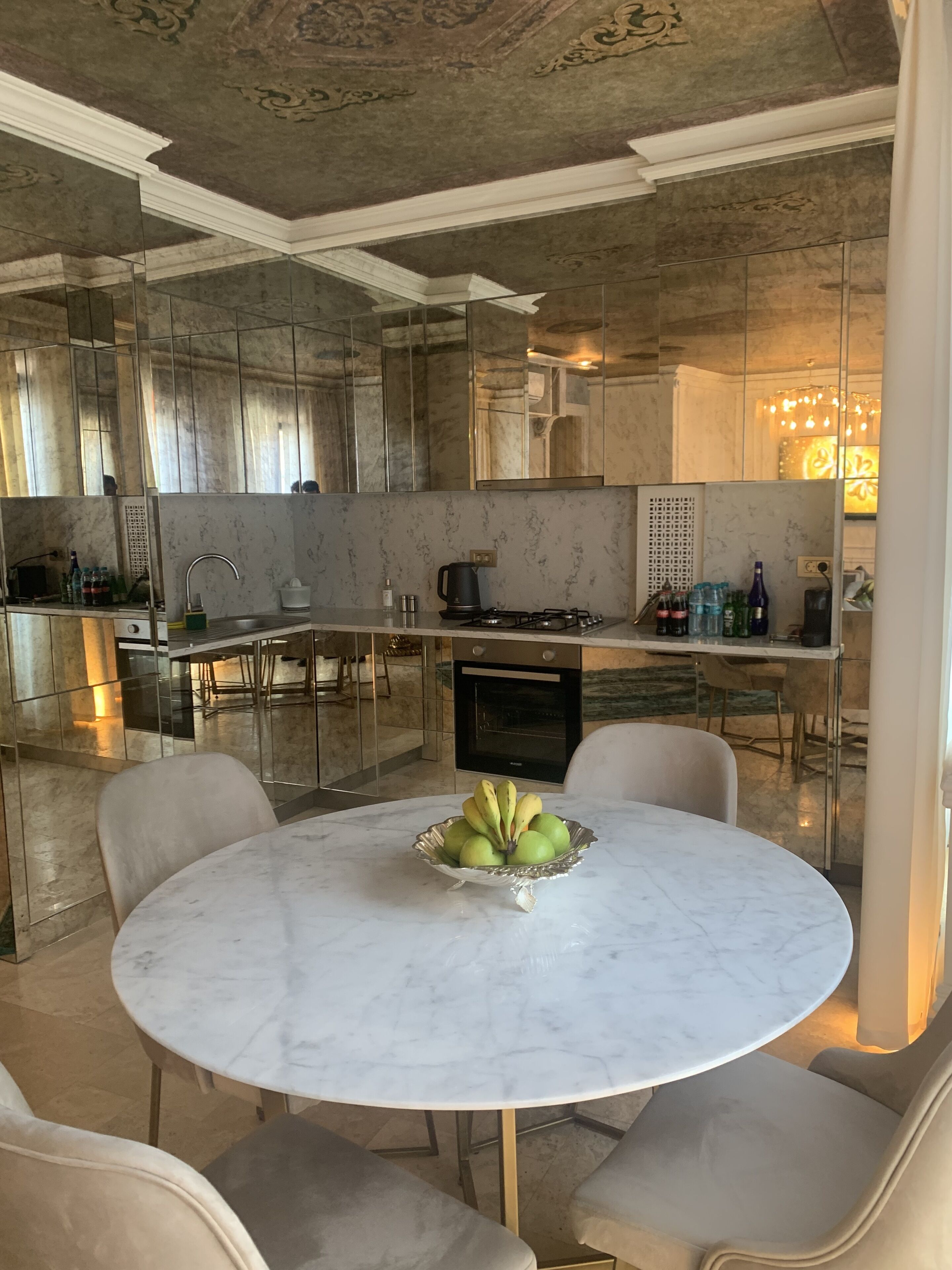 Uma cozinha moderna com bancada de mármore, uma mesa de jantar redonda com cadeiras e uma cesta de frutas.