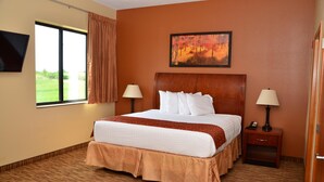 Quarto de hotel com uma cama grande, duas mesas de cabeceira com luminárias, um quadro na parede e uma janela com cortinas.