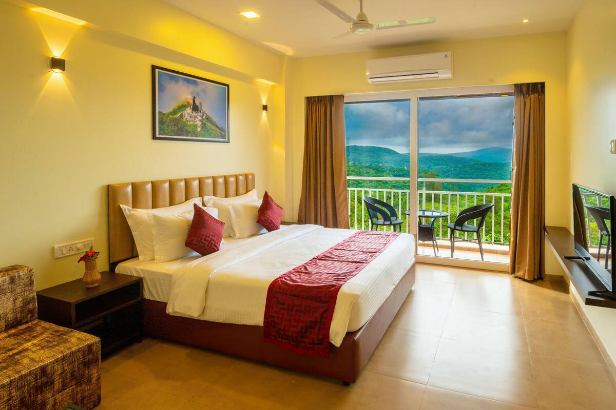Quarto de hotel com cama, mesa de cabeceira, cadeira e varanda com vista.