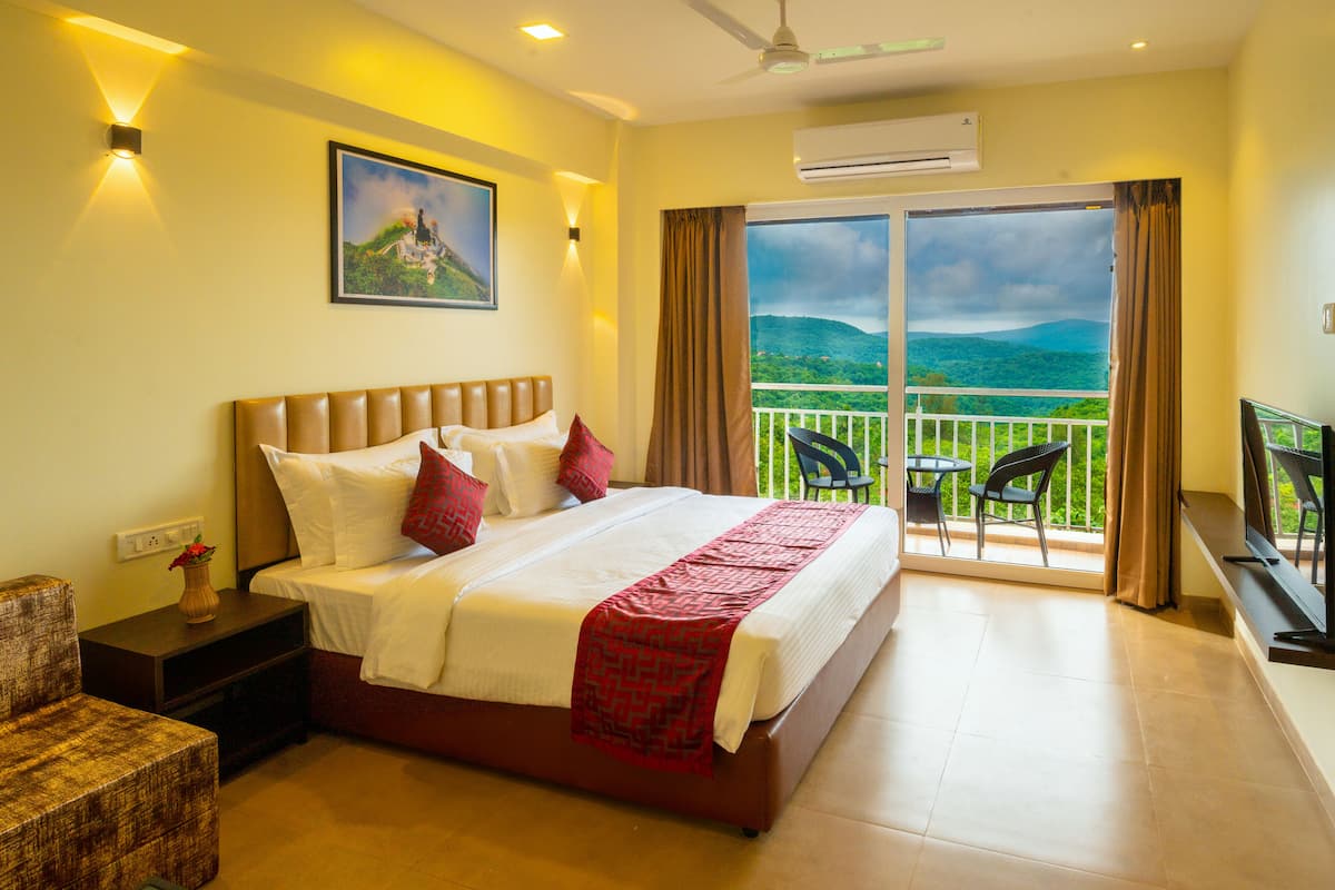 Quarto de hotel com uma cama grande, mesa de cabeceira, uma cadeira, varanda com vista para as montanhas e televisão.