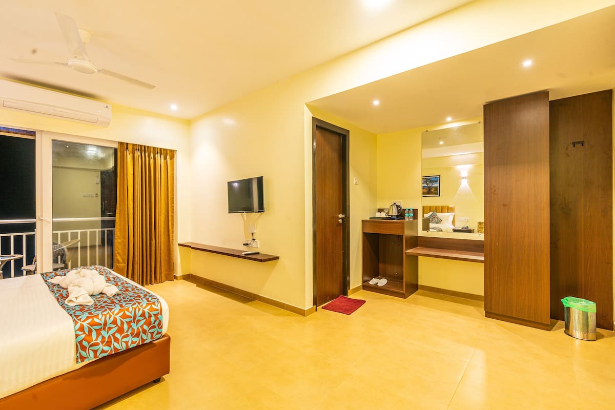Quarto de hotel com cama, televisão, escrivaninha, espelho e varanda.