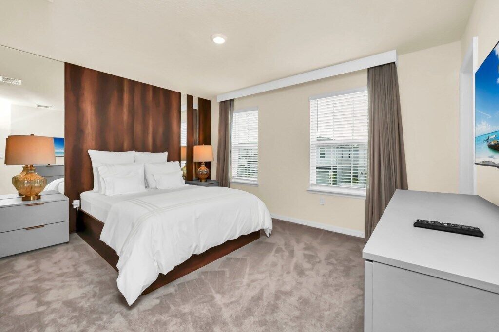 Quarto de hotel com uma cama grande, uma escrivaninha, uma luminária e um quadro na parede.