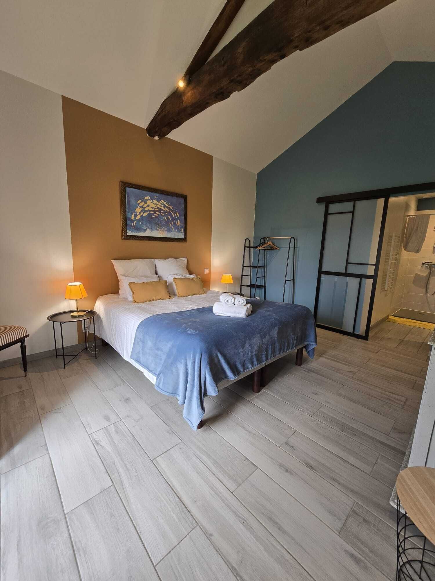 Quarto com cama, mesas de cabeceira, luminária pendente, quadro e área de chuveiro.