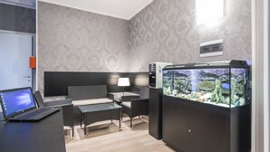 Um quarto moderno com um laptop sobre uma mesa, uma área de estar aconchegante com um sofá e poltronas, e um aquário grande na parede.