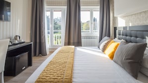 Quarto de hotel moderno com uma cama grande, uma escrivaninha com chaleira e vista para o exterior por grandes janelas.