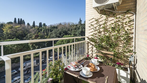 Varanda com mesa posta para o café da manhã, vista para uma estrada e vegetação.