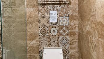 Casa de banho com sanita, chuveiro e azulejos estampados.