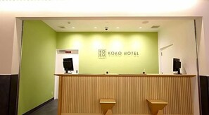 Balcão de recepção com uma placa indicando "KOKO HOTEL" e uma câmera de segurança acima.