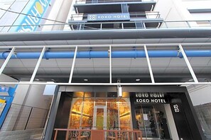 Um hotel com fachada moderna, um letreiro em destaque com a inscrição "KOKO HOTEL" e entrada de vidro.