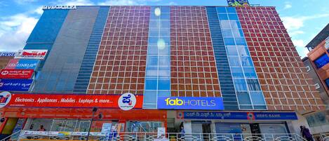 Um hotel com fachada moderna, vários andares e diferentes placas, incluindo 'fab hotels' e 'raymond'.