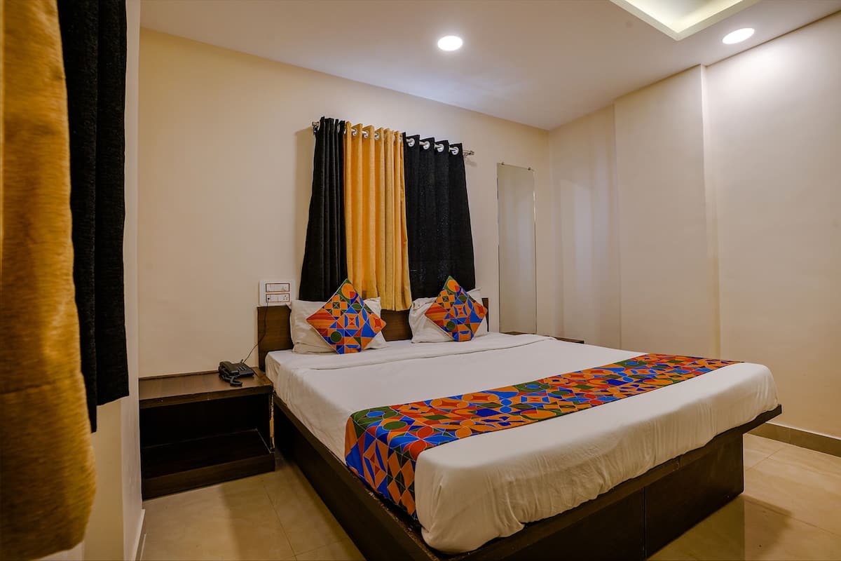 Quarto de hotel com uma cama grande, uma mesa de cabeceira com telefone e cortinas.