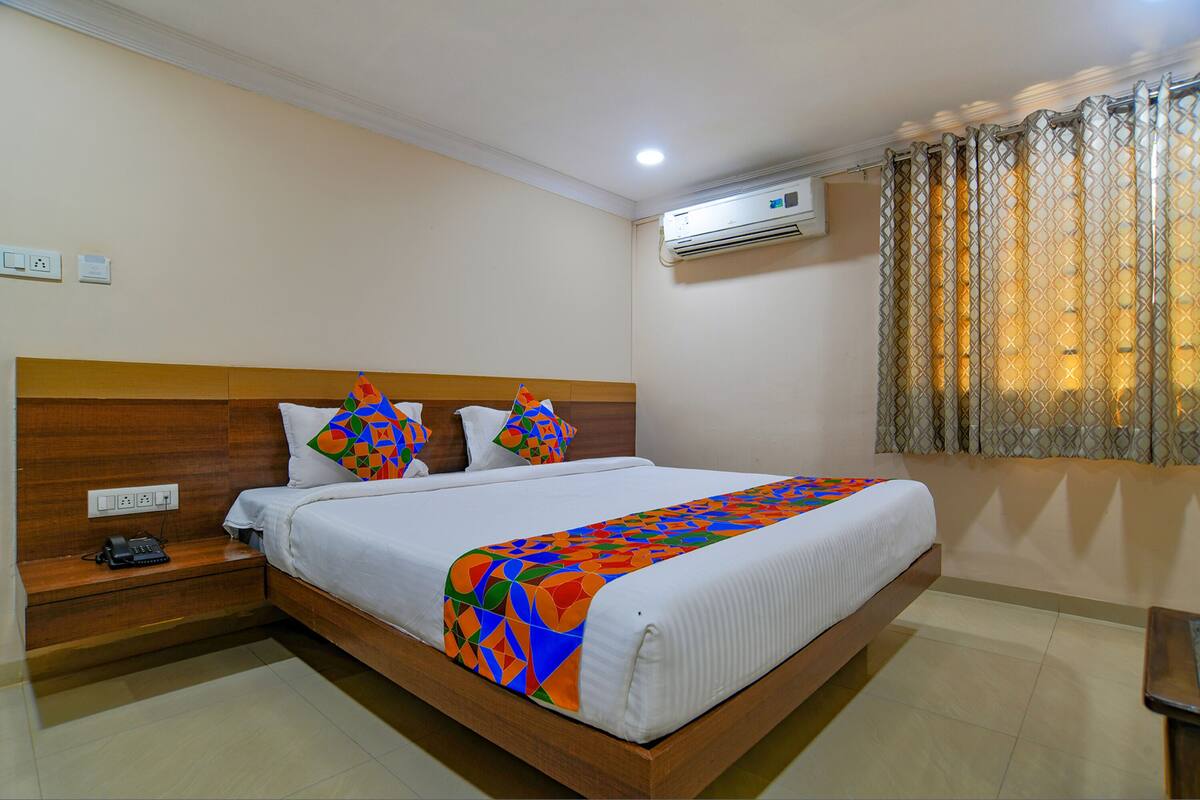 Uma cama bem arrumada com um cobertor colorido, uma cabeceira de madeira e uma mesinha de cabeceira com um telefone.