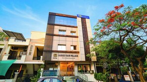 Um hotel de vários andares com fachada moderna, um letreiro com 'Free Ram Palace Hotel' e uma árvore com flores vermelhas à direita.