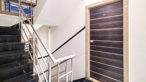 Um interior moderno com uma escada, uma porta de madeira escura com a inscrição '201' e uma janela com persianas.