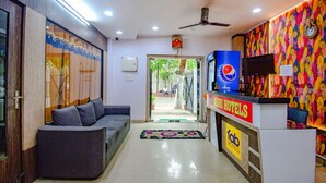 Uma área de recepção de hotel com um sofá, um refrigerador da Pepsi, um relógio e uma parede colorida.
