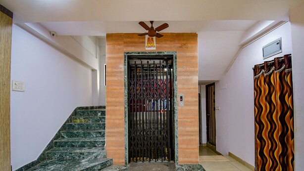 Escadaria que leva a um elevador, com portão de metal, ventilador de teto e cortina estampada.