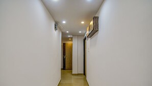 Um corredor estreito com paredes brancas, luzes embutidas no teto e uma porta de madeira no final.