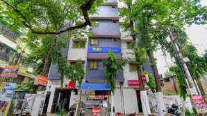 Um edifício de vários andares com a sinalização 'Adri Hotels', rodeado por vegetação e outros estabelecimentos.