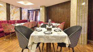 Uma área de refeições com uma mesa posta para quatro pessoas, cercada por cadeiras vermelhas estofadas com estampas florais.