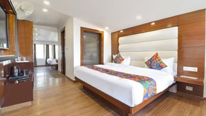 Quarto de hotel com uma cama grande, cabeceira de madeira e mesa de cabeceira com chaleira e cafeteira.