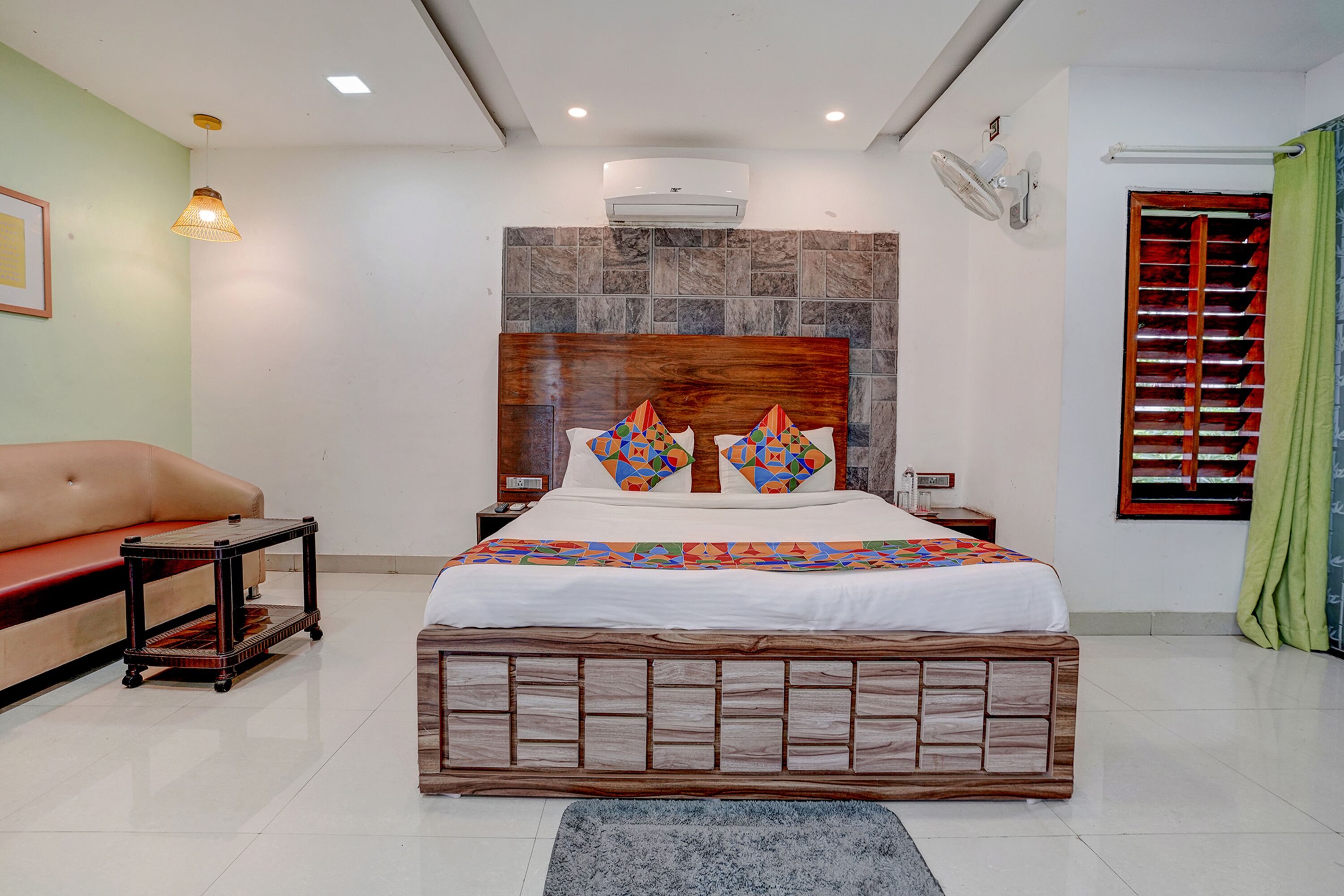 Quarto com cama grande, mesa de cabeceira, ar condicionado fixado na parede e janela com cortinas.