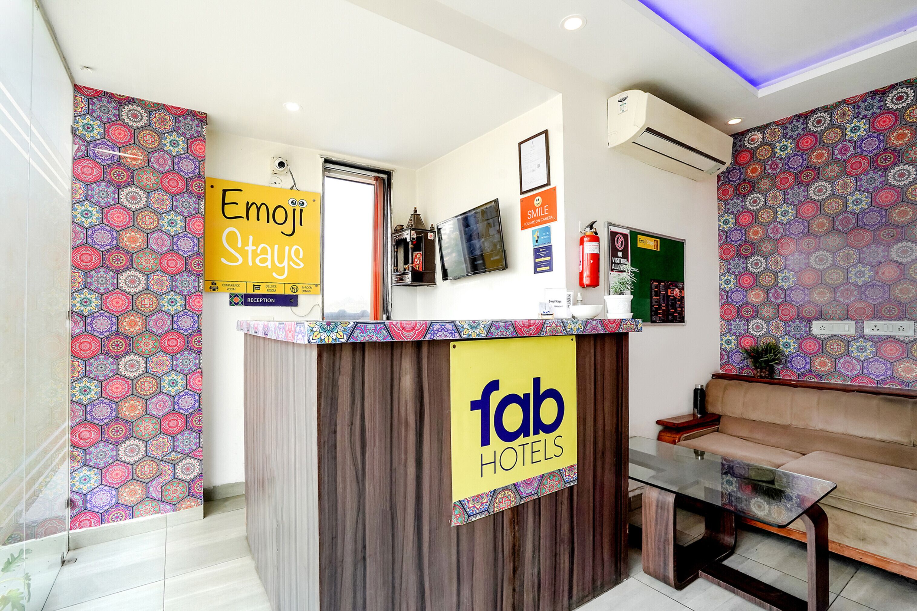 Uma mesa de recepção com o letreiro 'fab hotels', uma área de recepção com uma televisão, um extintor de incêndio e um papel de parede estampado.
