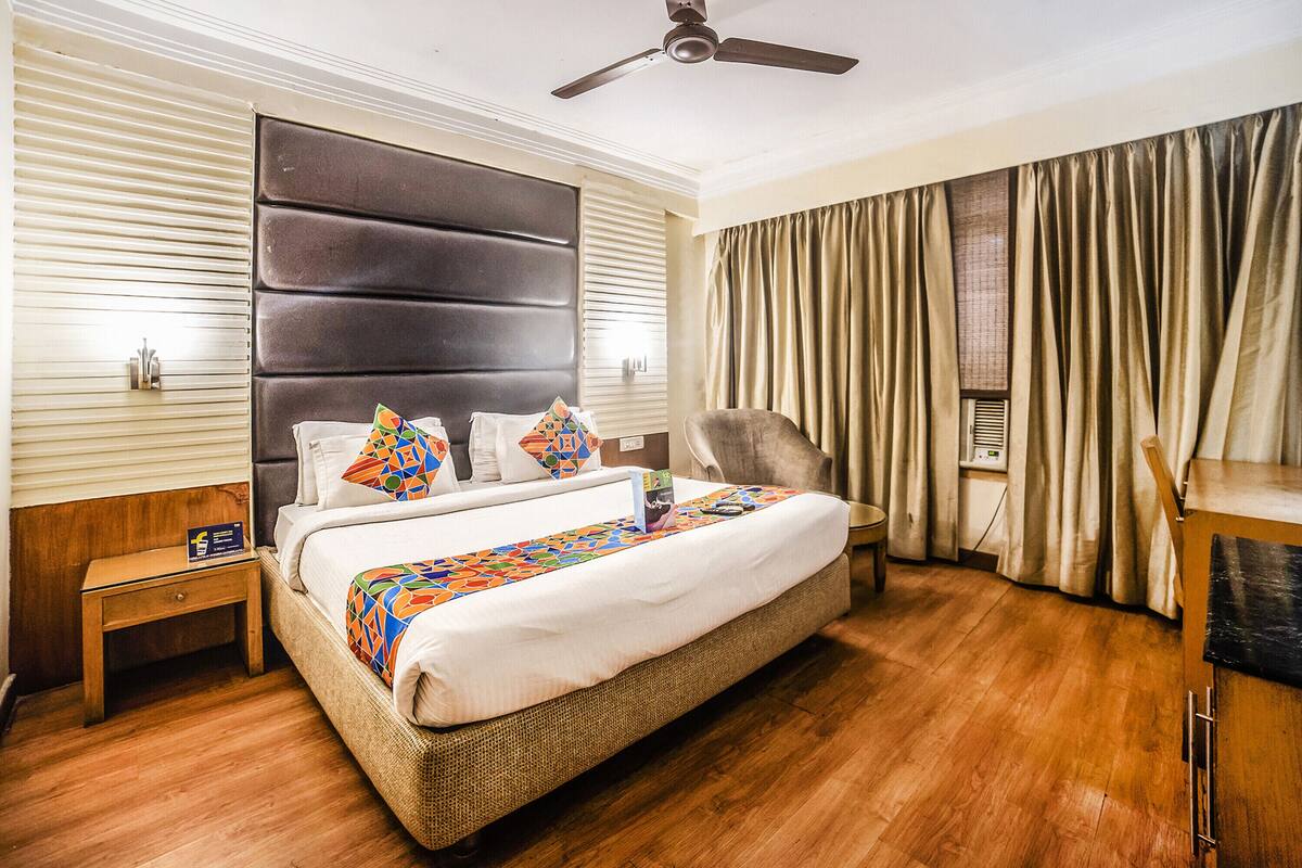 Quarto de hotel com cama grande, mesa de cabeceira de madeira, cadeira e ventilador de teto.