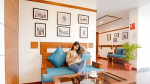Um saguão de hotel com um banco de madeira, uma mesa de centro de vidro e quadros nas paredes.