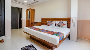 Quarto de hotel moderno com uma cama grande, cabeceira de madeira e um edredom colorido.