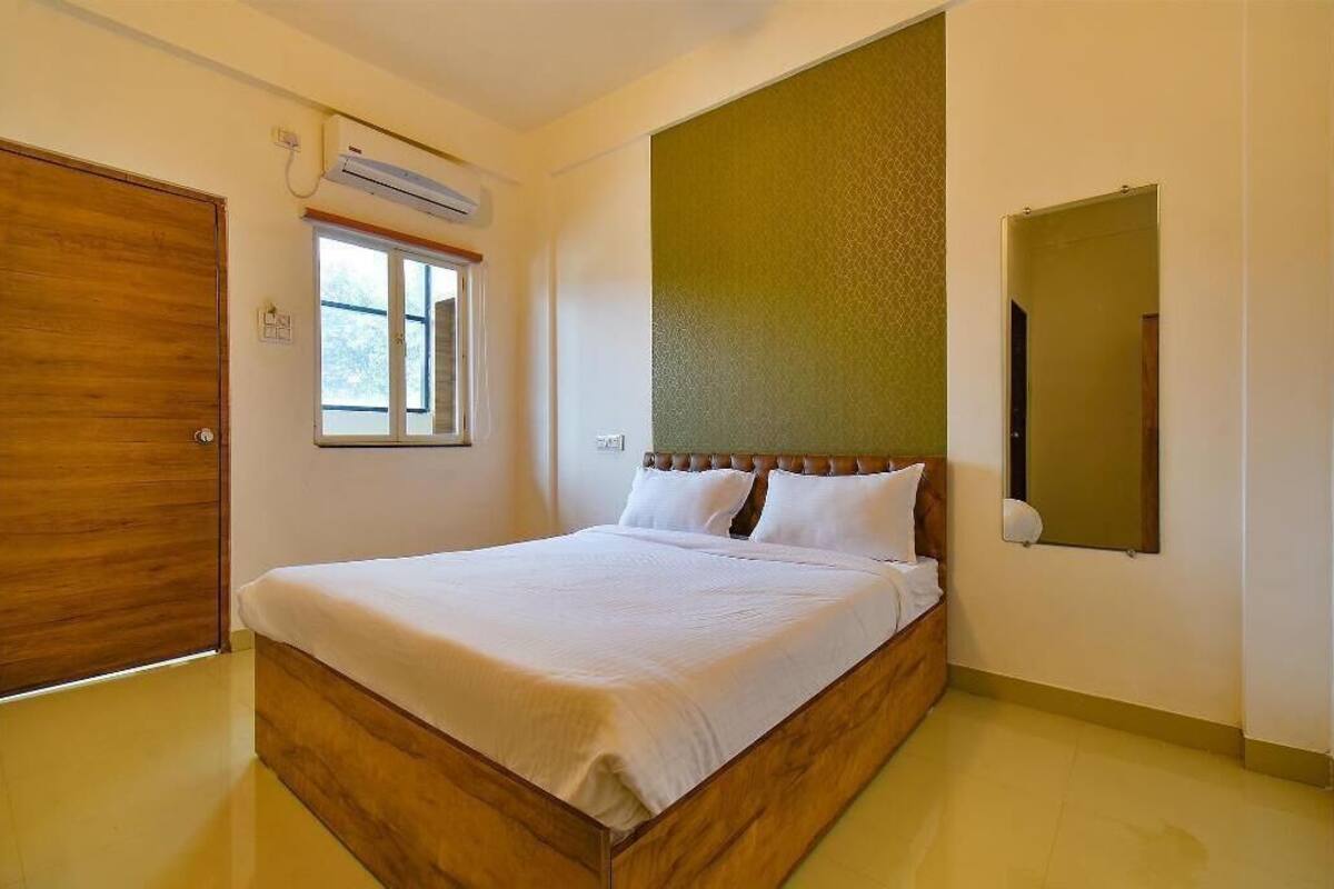 Quarto com cama de madeira, janela, aparelho de ar condicionado e parede verde com textura.