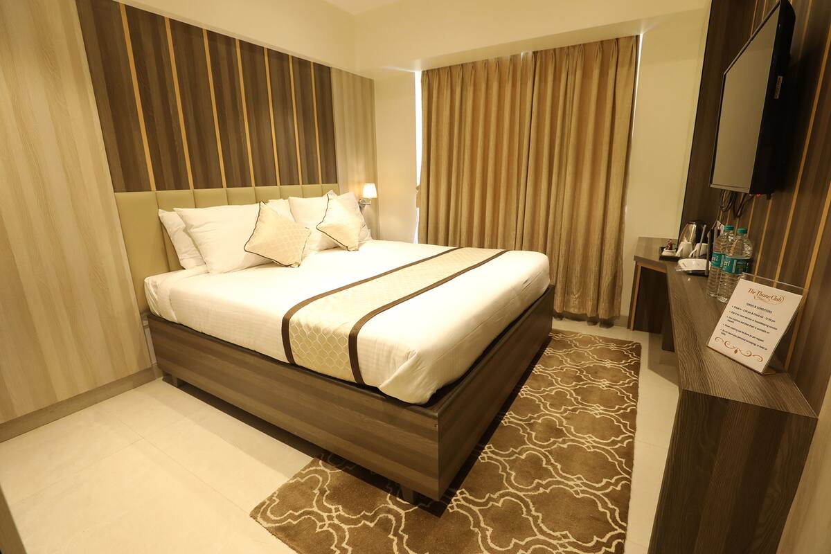 Quarto de hotel com uma cama grande, cabeceira de madeira, mesa de cabeceira com espelho e placa indicando o tipo de quarto.