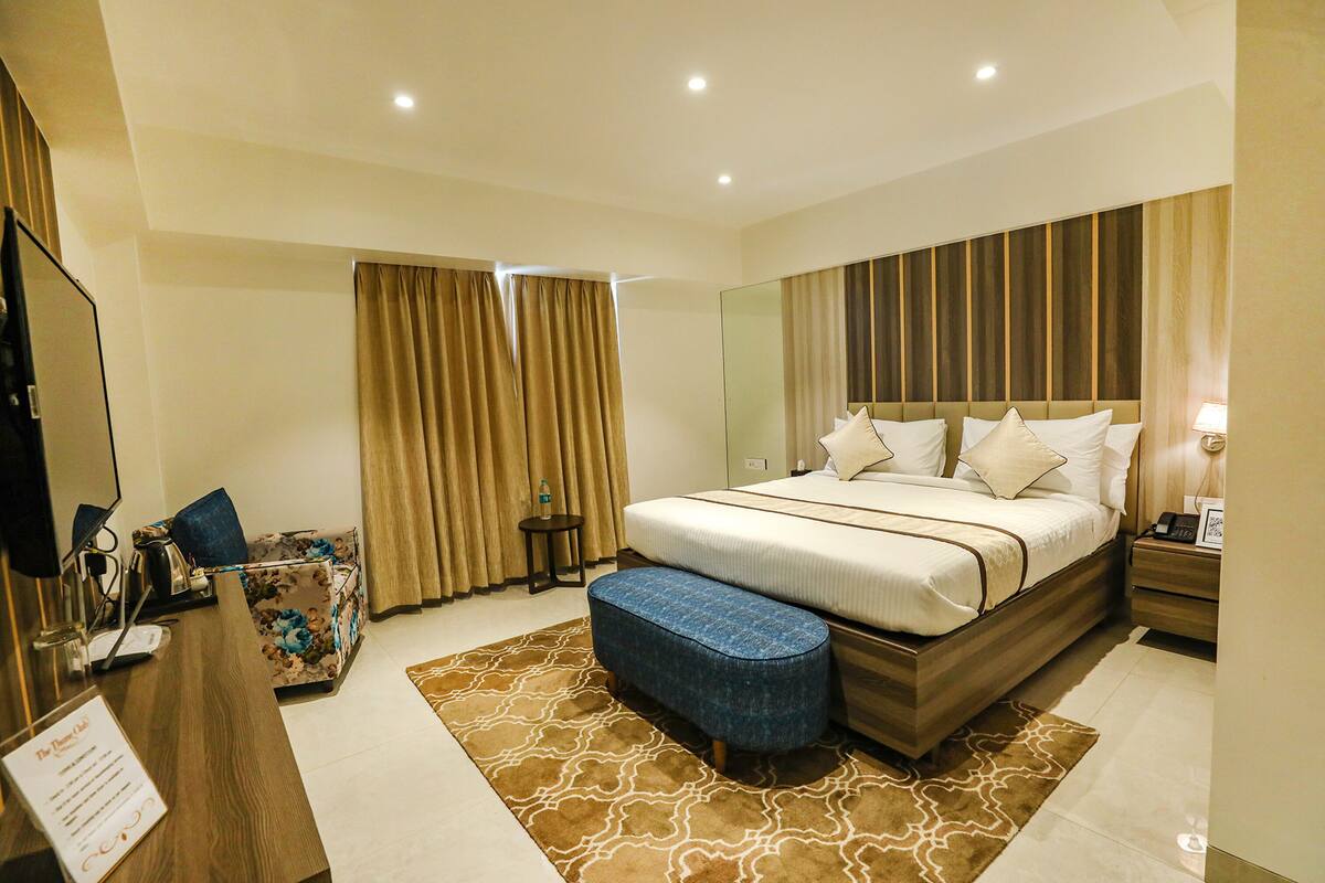 Quarto de hotel com uma cama grande, uma escrivaninha com cadeira, uma mesinha e um espelho.
