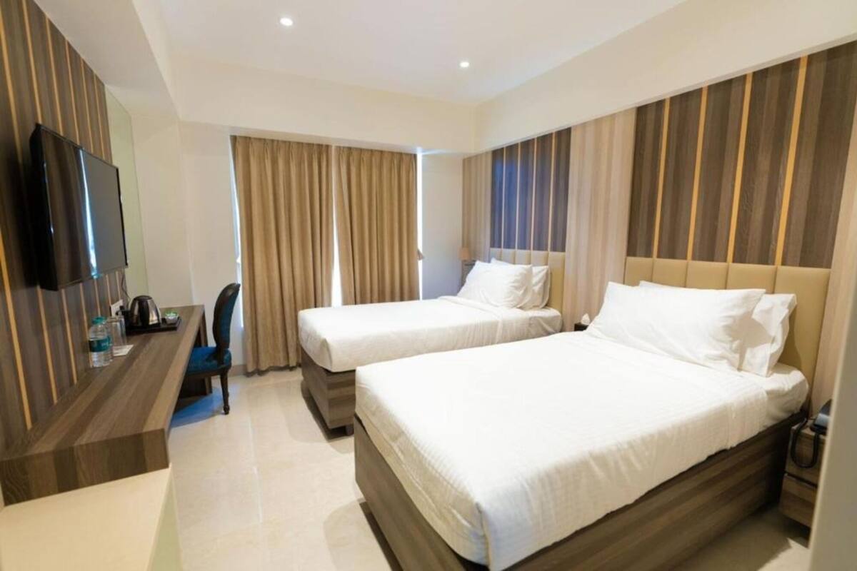 Quarto de hotel com duas camas, uma mesa de trabalho e uma televisão de tela plana, além de uma cadeira.