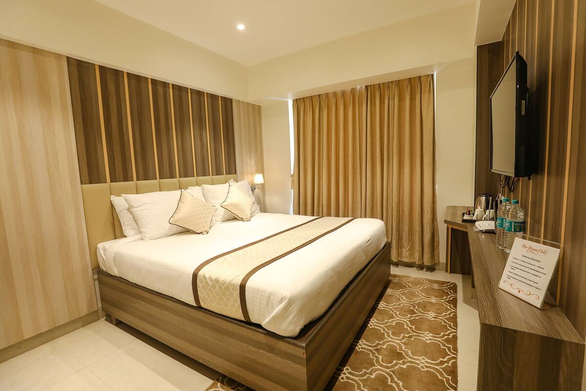 Quarto de hotel com uma cama grande, cabeceira de madeira, televisão de tela plana, escrivaninha com cadeira e uma placa.
