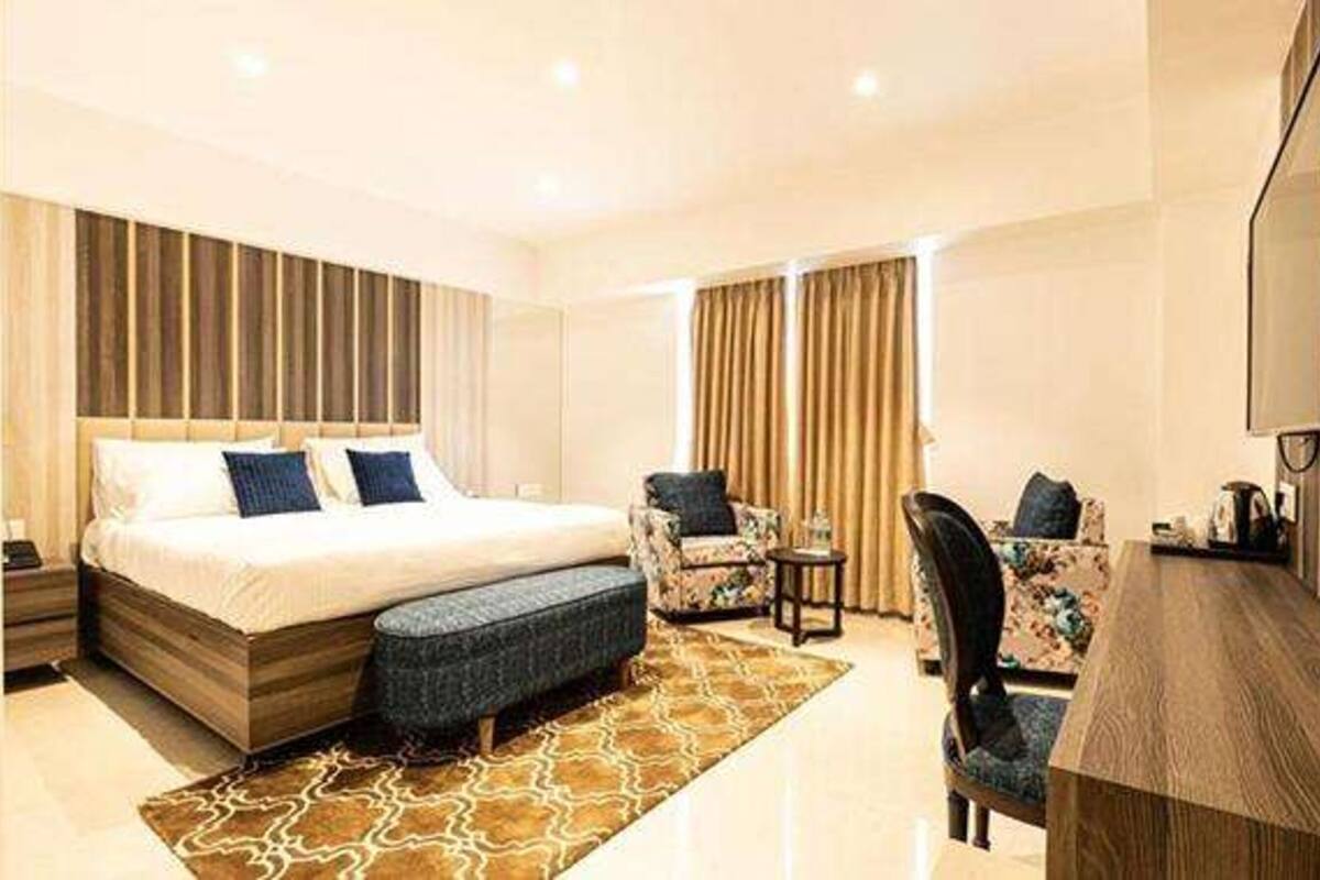 Quarto de hotel com cama, escrivaninha, cadeira e televisão.