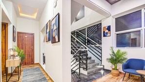 Um interior moderno com piso de madeira, um sofá azul, uma escada e arte abstrata nas paredes.