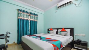Uma cama bem arrumada com um edredom colorido, uma mesa de cabeceira com um telefone e cortinas cor turquesa.